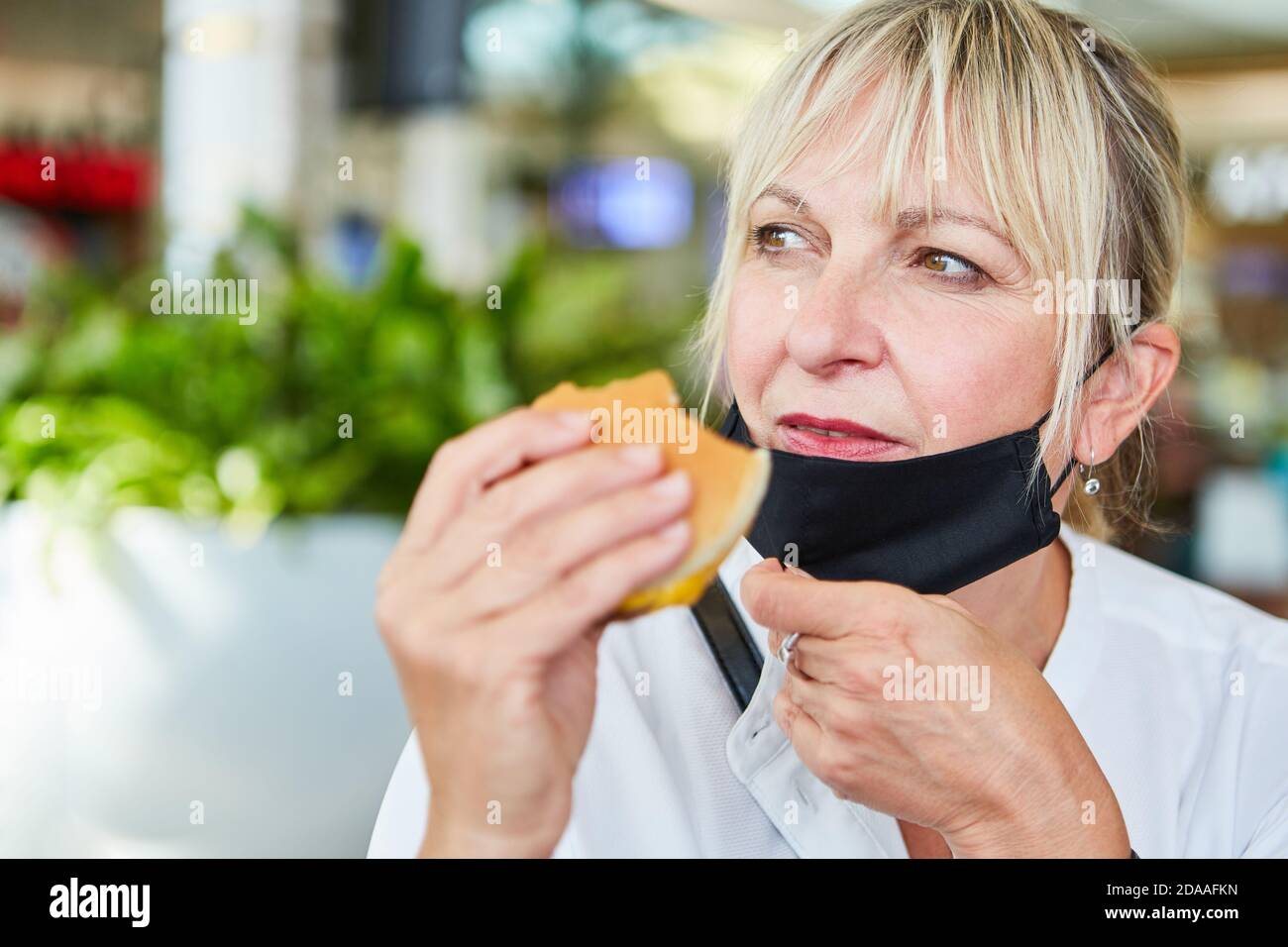 Woman as a guest with a face mask on her chin while eating a burger in ...