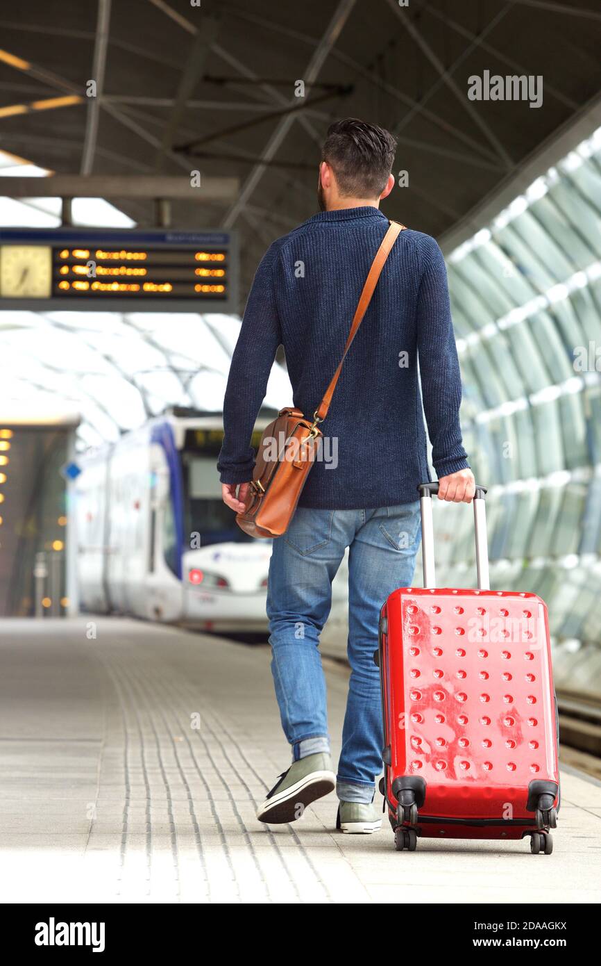Rear view full body portrait of man walking on train station platform ...