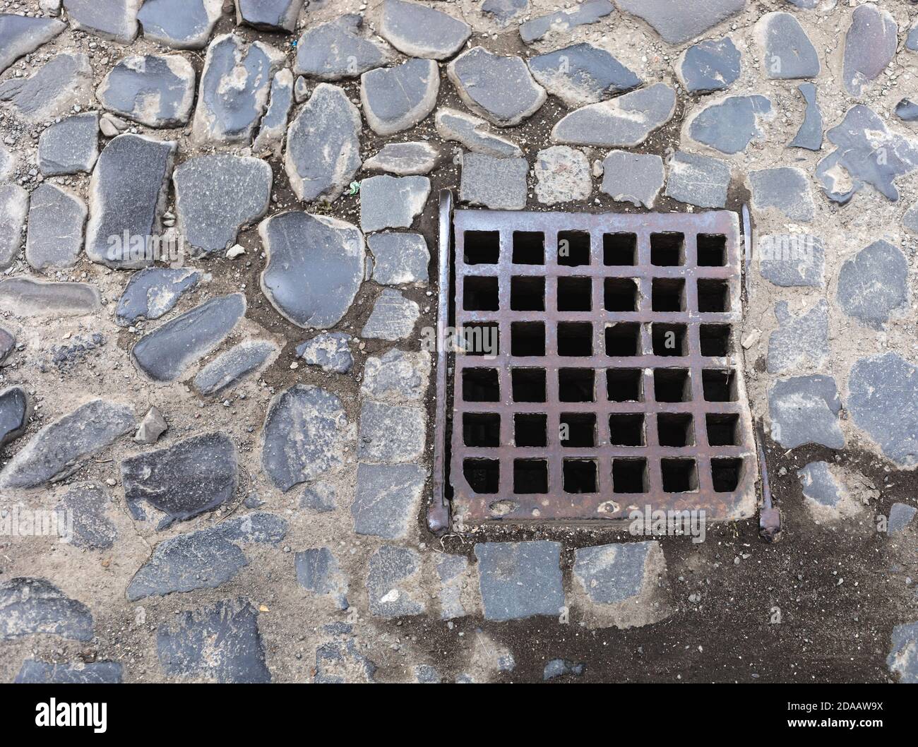 Old iron grate of the drainage system hatch on the road paved with ...
