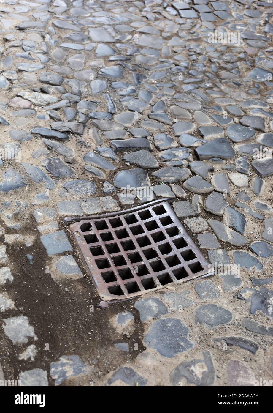 Old iron grate of the drainage system hatch on the road paved with ...