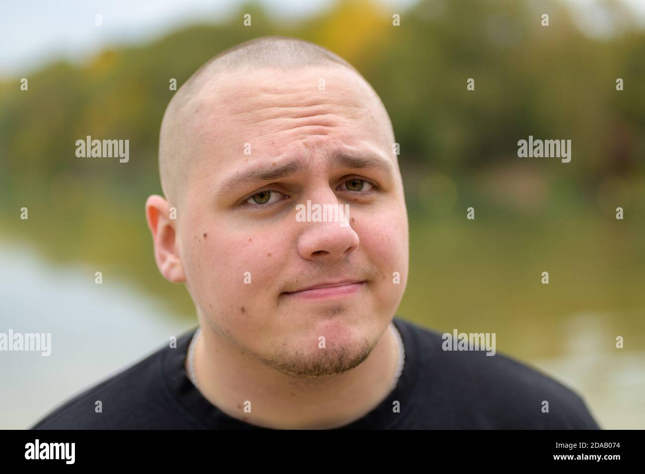 Close up frontal head shot of a thoughtful young man with shaved head ...