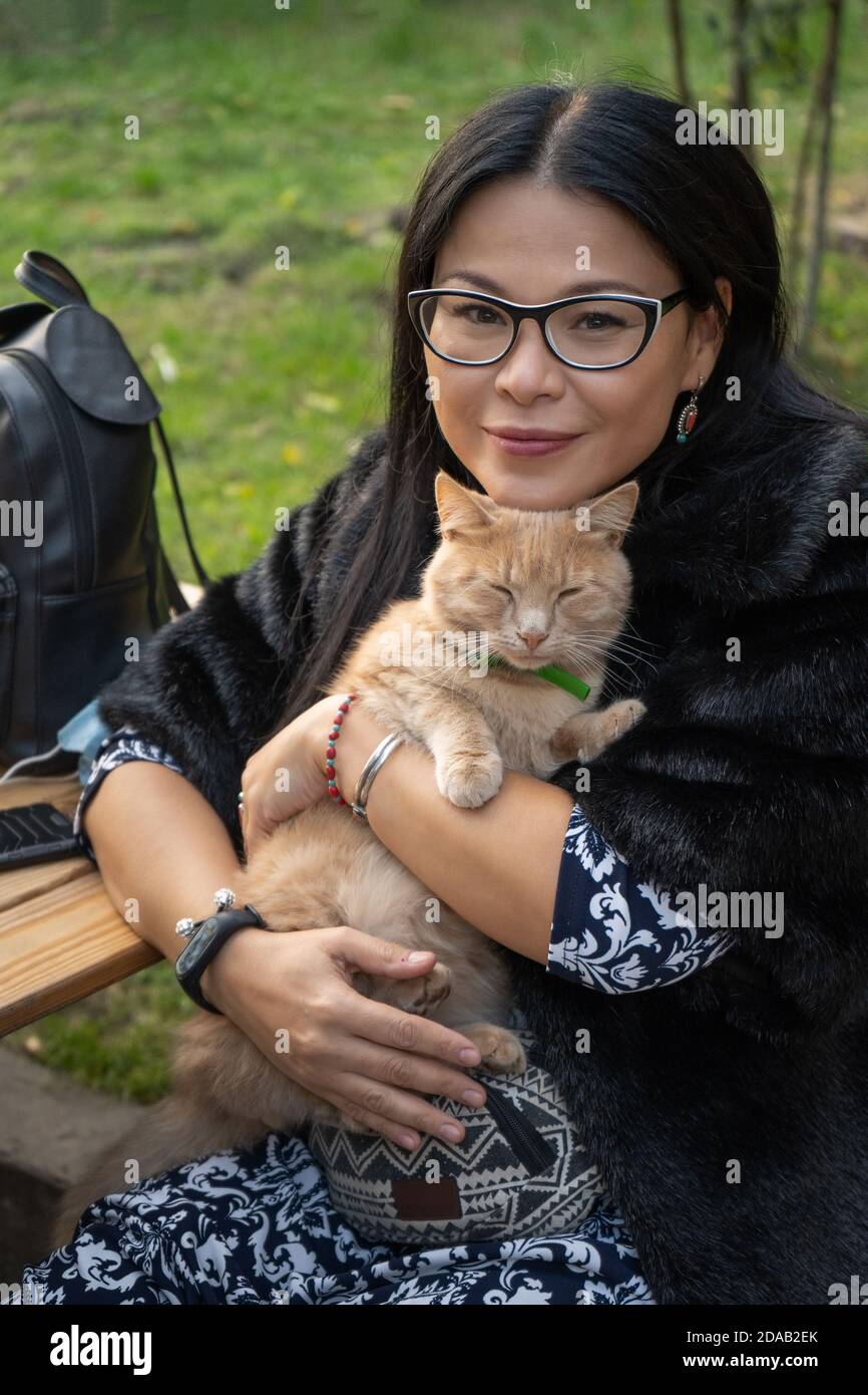 Middle-aged woman hugs cat while resting on street bench outdoors ...