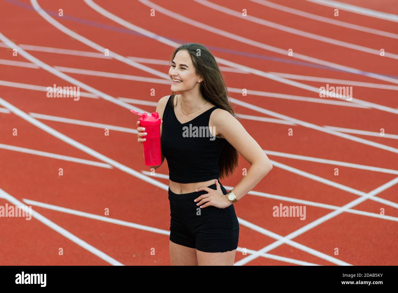 A female coach with dark hair stands on the red running track of the ...