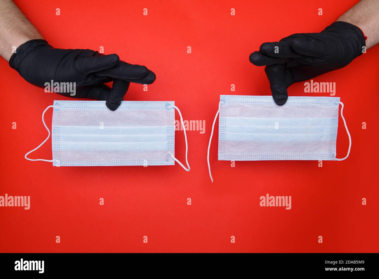 hands in black latex gloves hold two medical masks, one with torn ...