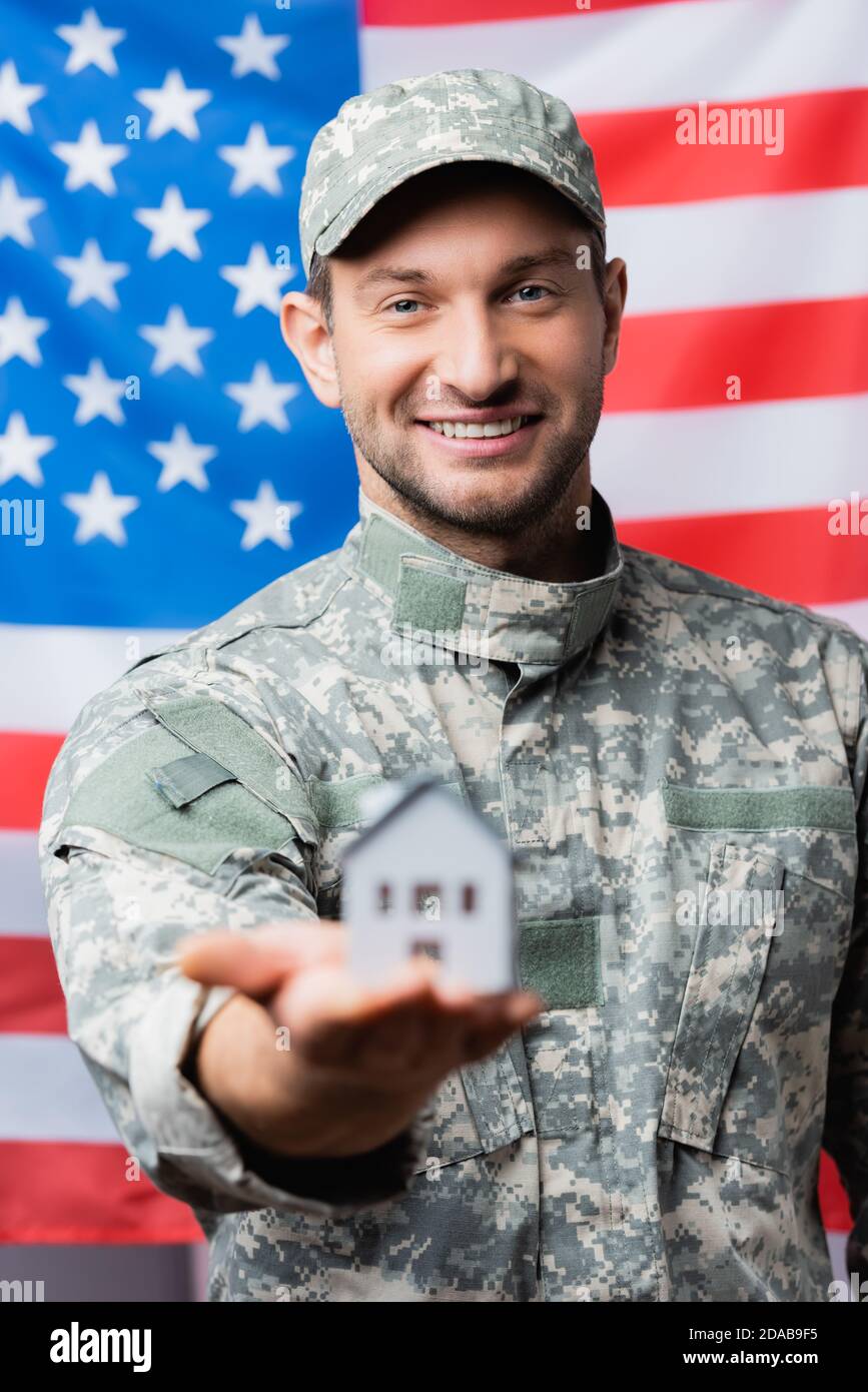 happy military man in uniform holding house model near american flag on ...
