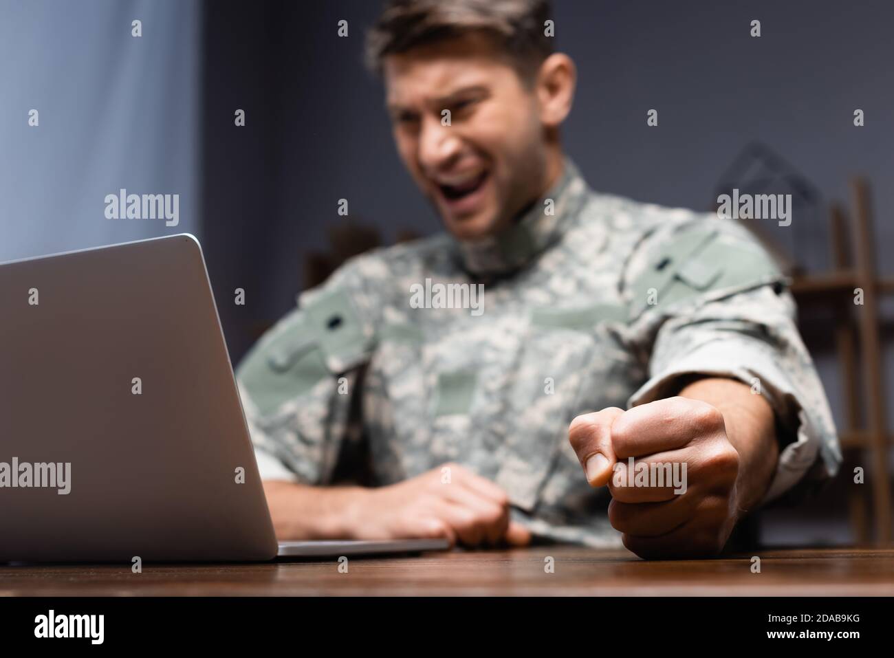 angry military man in uniform sitting with clenched fist near laptop on ...