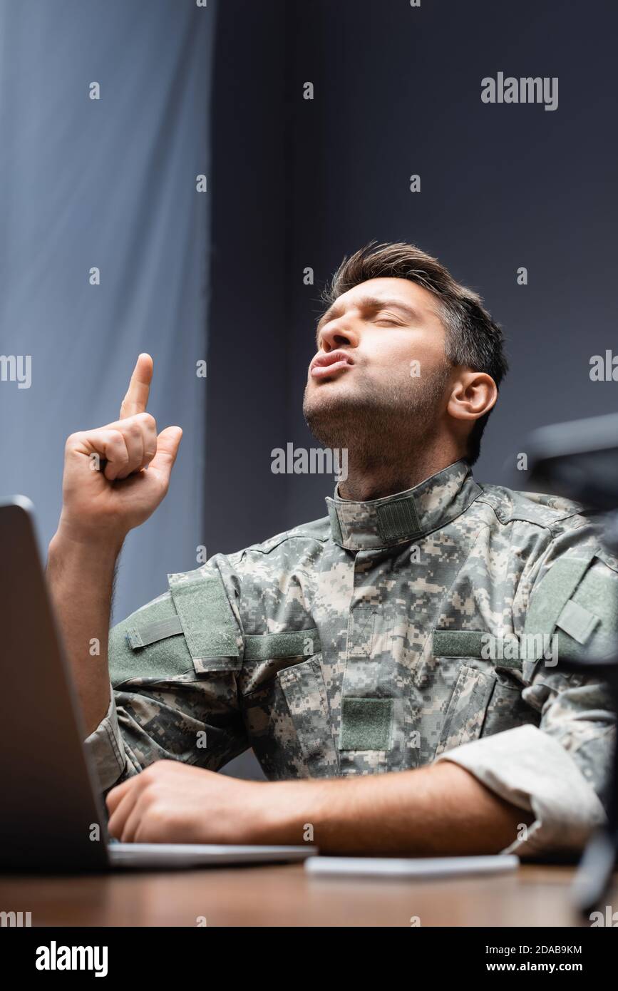 military man in uniform talking and pointing with finger near laptop on ...
