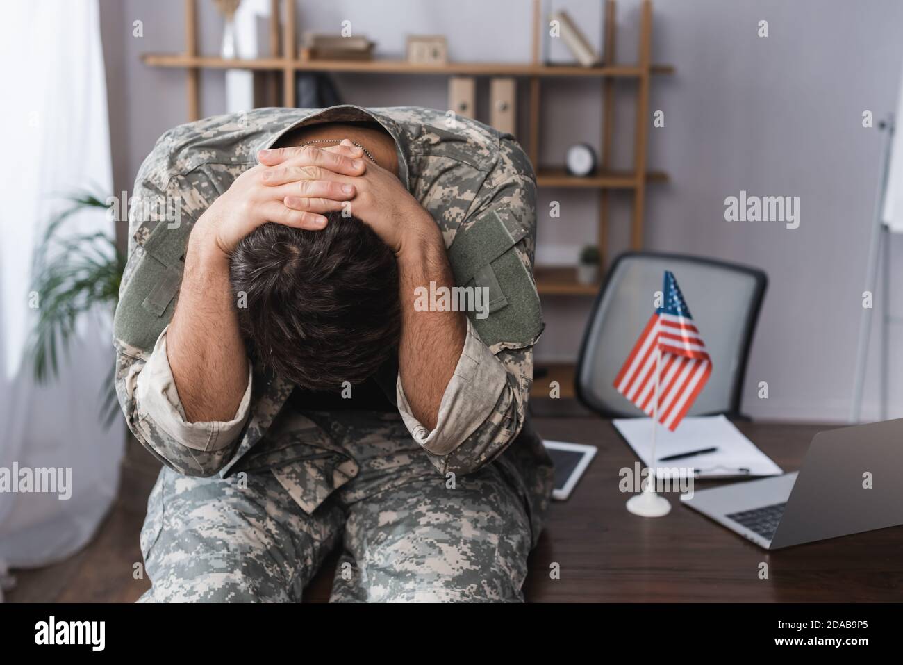 military man sitting on desk and leaning near gadgets and american flag ...