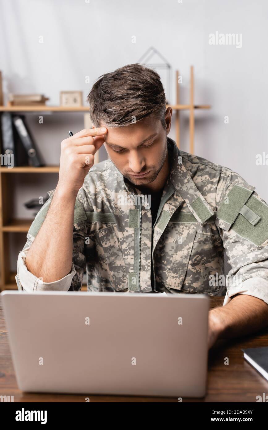 pensive soldier in uniform sitting at desk and using laptop Stock Photo ...