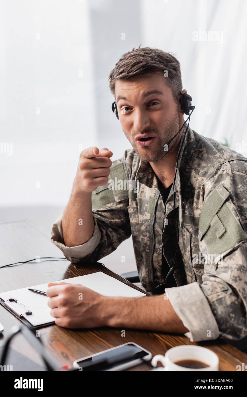 military man in uniform and headset talking while pointing with finger ...