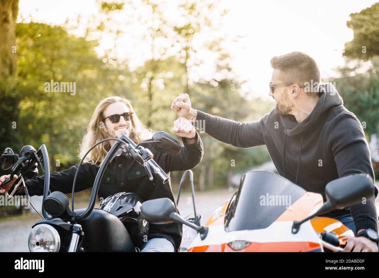 Two young men waving at each other while sitting on two motorcycles ...