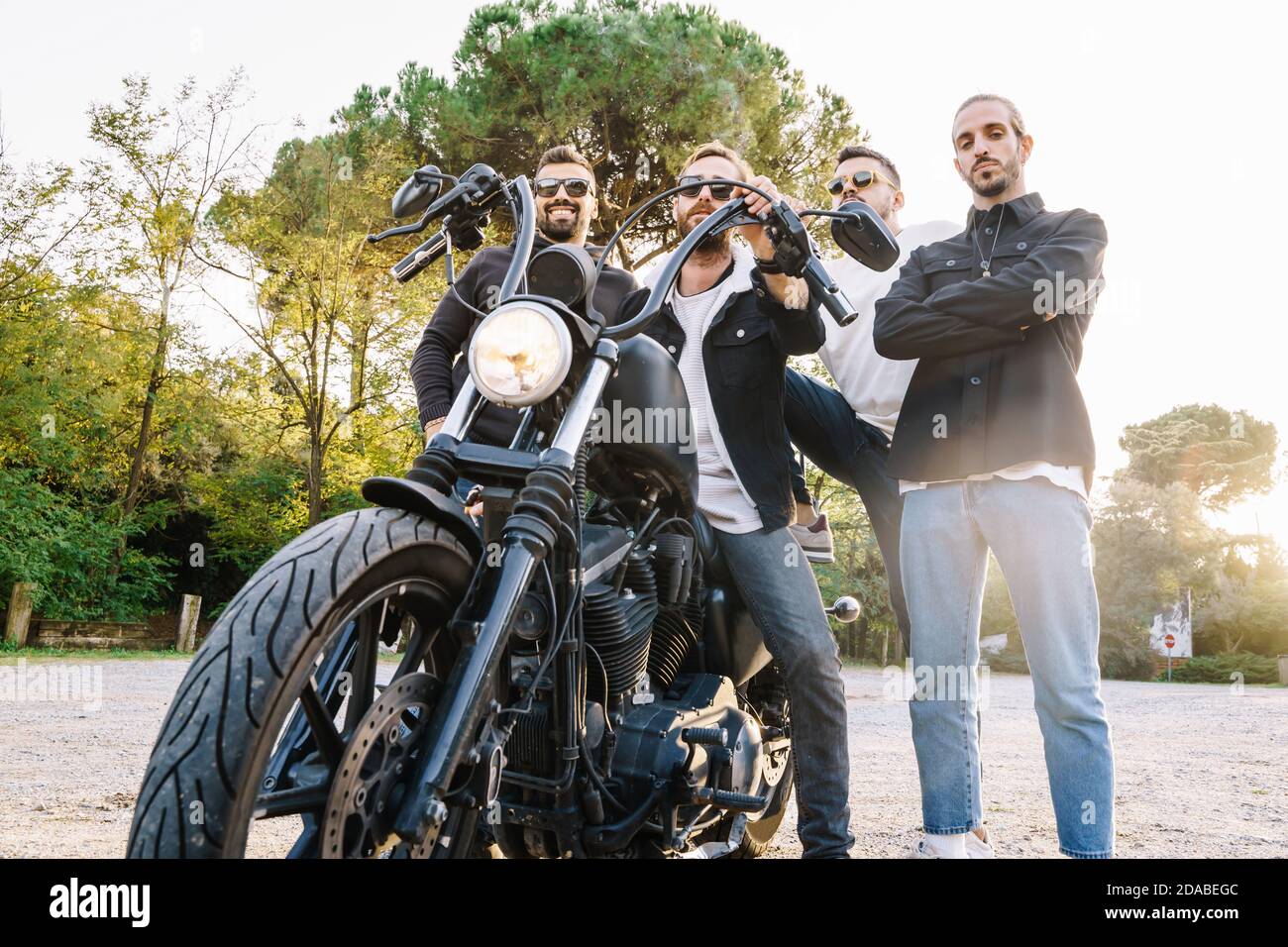 Three men standing next to a biker in a parking lot surrounded by trees ...