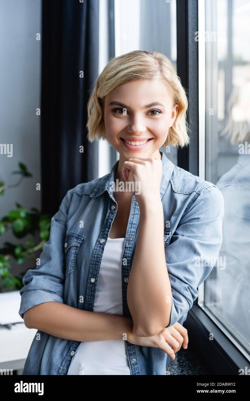 portrait of smiling blonde woman standing near window Stock Photo - Alamy