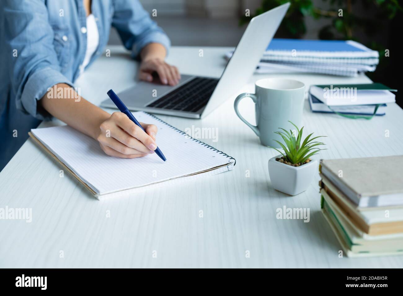 cropped view of woman making notes in notebook and typing on laptop ...