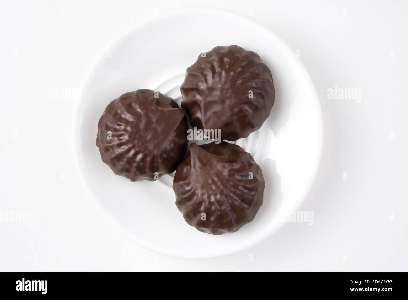 Three marshmallows covered with icing in a white plate on a light ...
