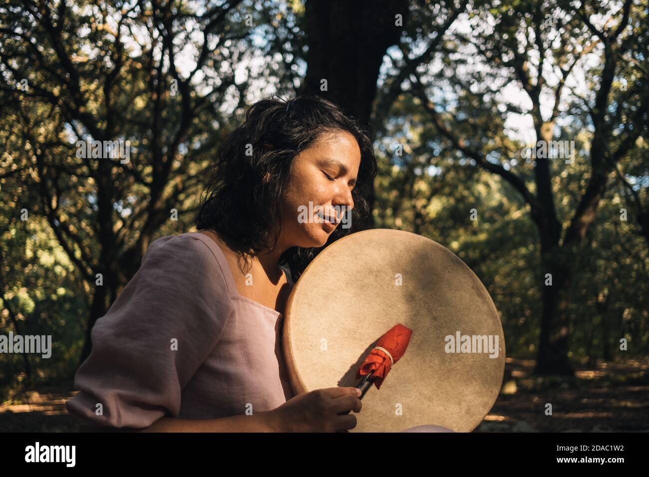 young woman playing tambour in the woods in nature with incense. mystic ...