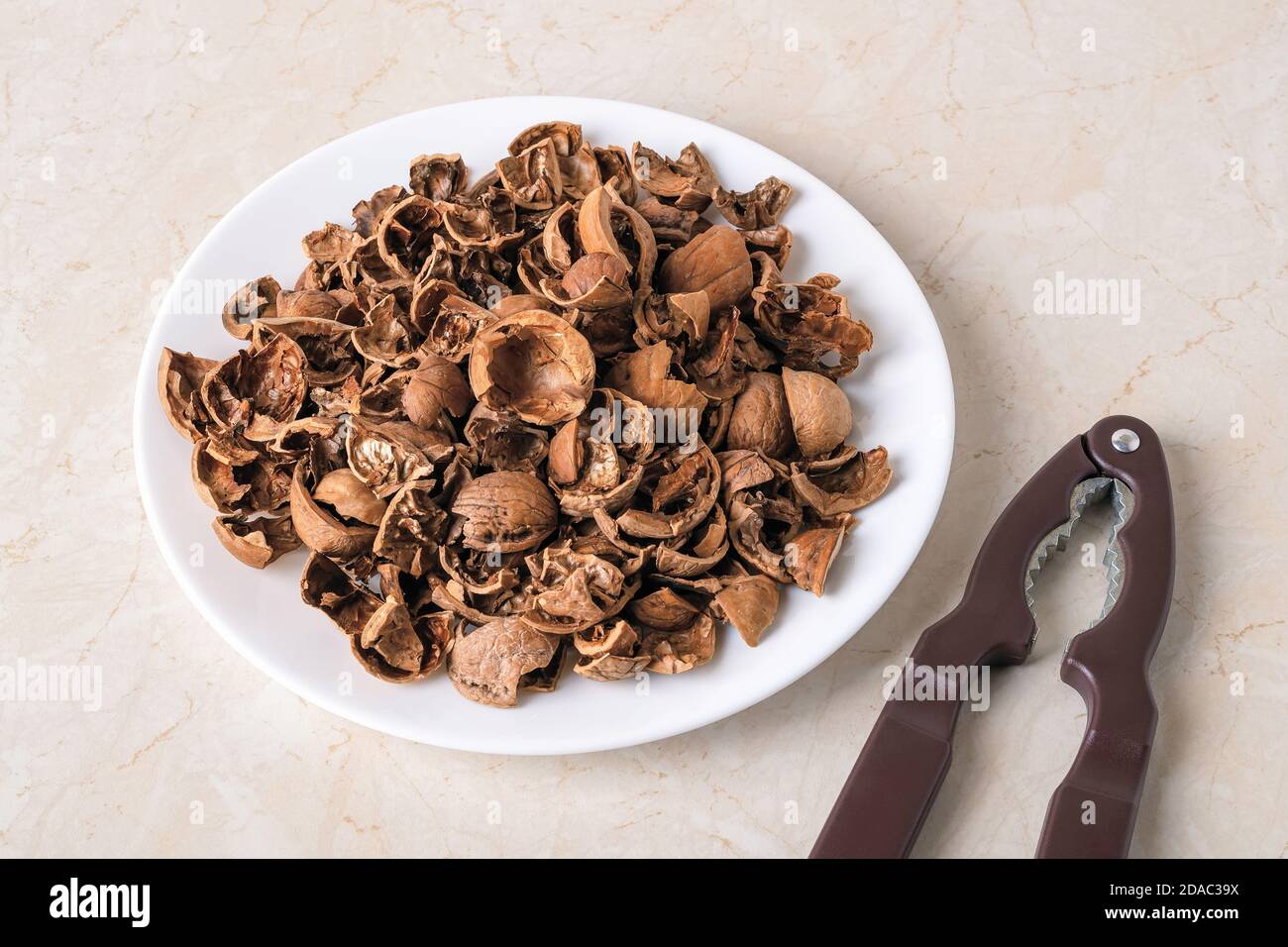 Pile of empty broken walnut shells on a white plate and nutcracker over ...