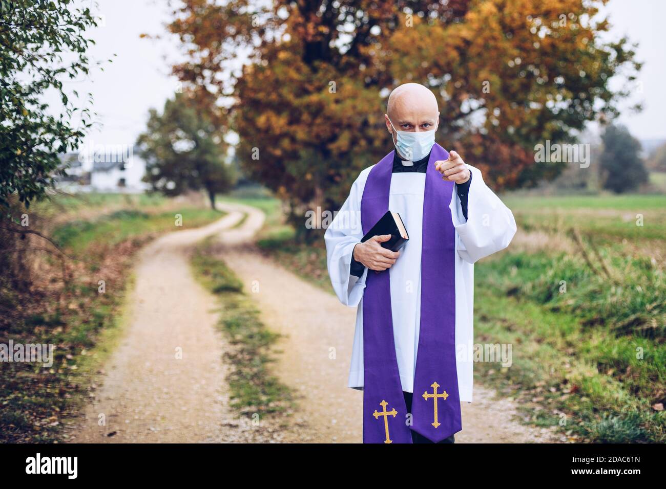 Catholic priest with a bible in a medical mask points with his finger ...