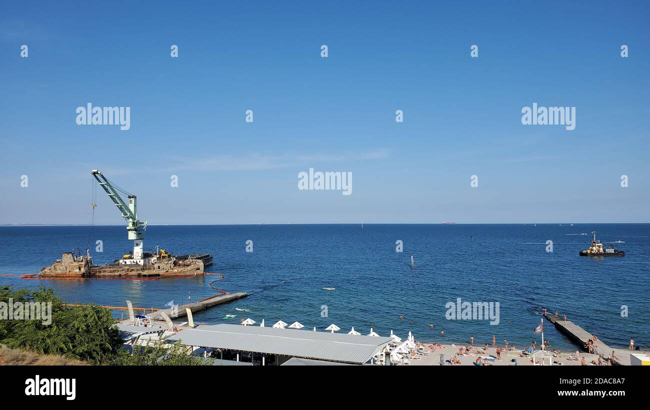 Wrecked cargo ship lies on side near coastline with sandy beach ...