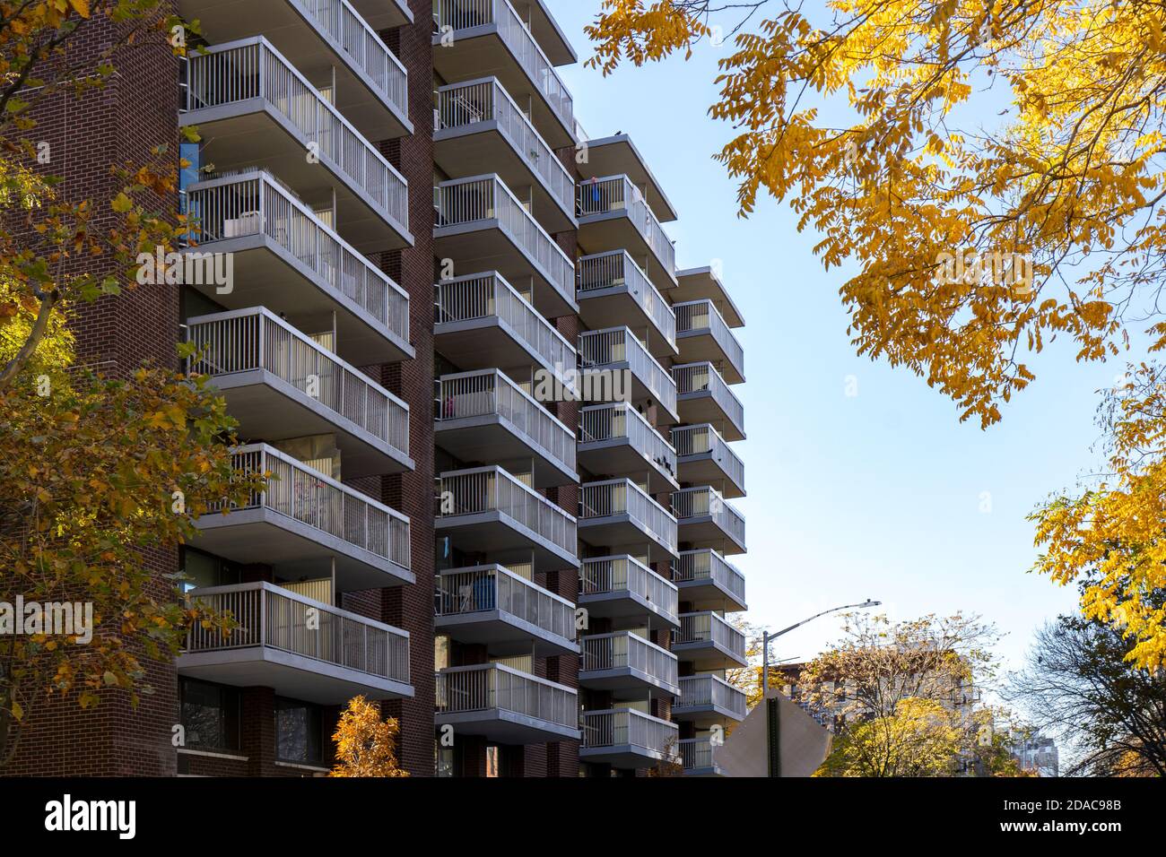 Apartment brick building with balconies for each unit. Trees with ...
