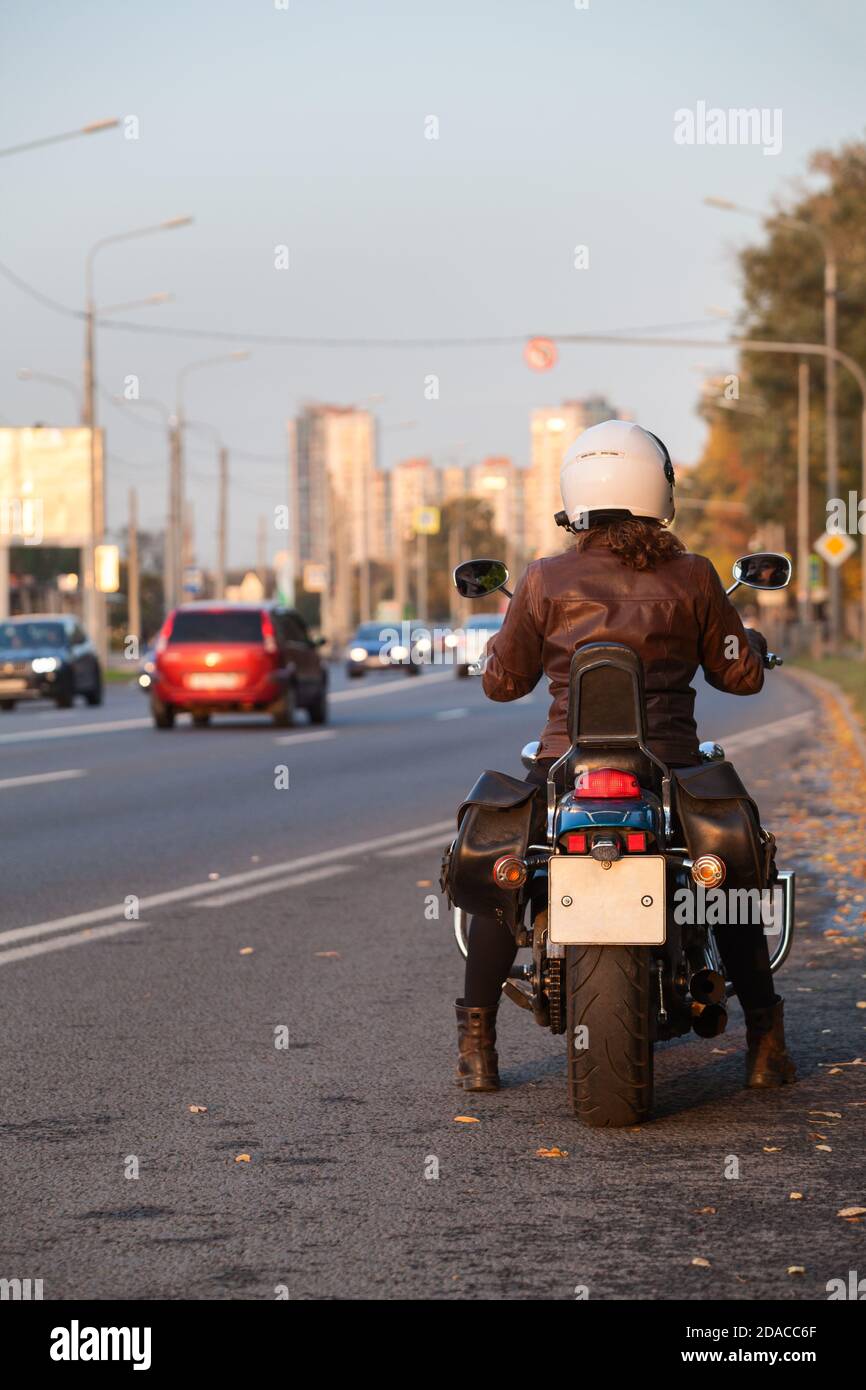 Rear view at motorbiker with motorcycle standing on urban road, female ...