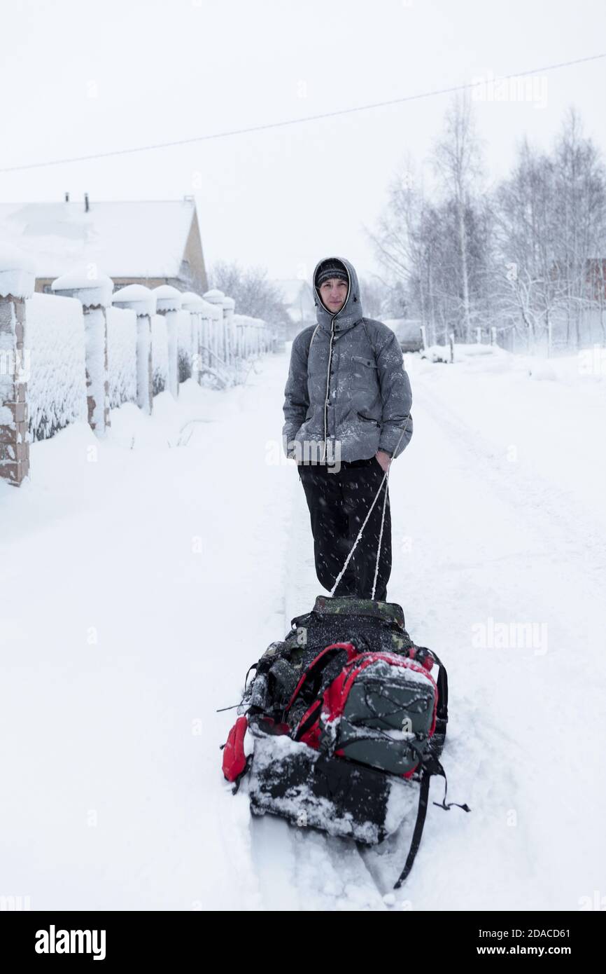 Adult Caucasian man portrait stands with drag sled in the snowy village ...