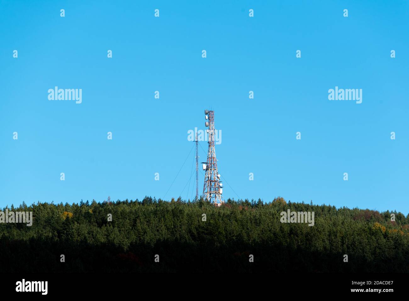 A telecommunications tower on top of forest hill with clear blue sky ...