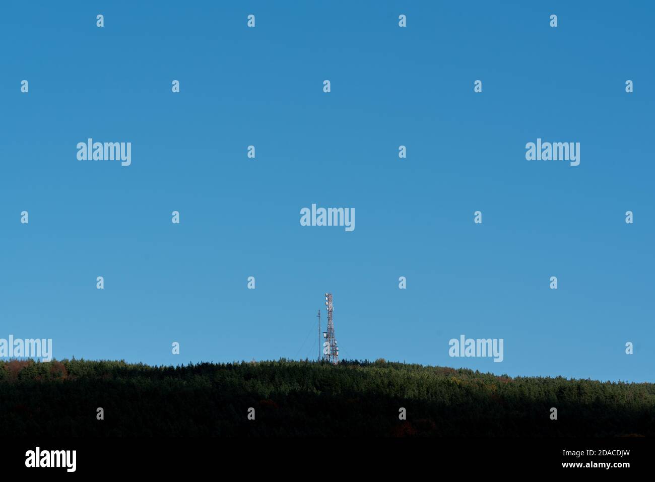 A telecommunications tower on top of forest hill with clear blue sky ...