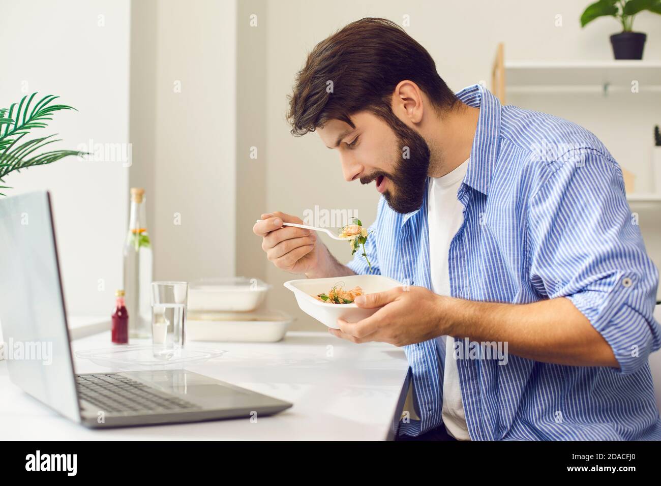 Young man sitting at workplace and eating healthy balanced delivered ...