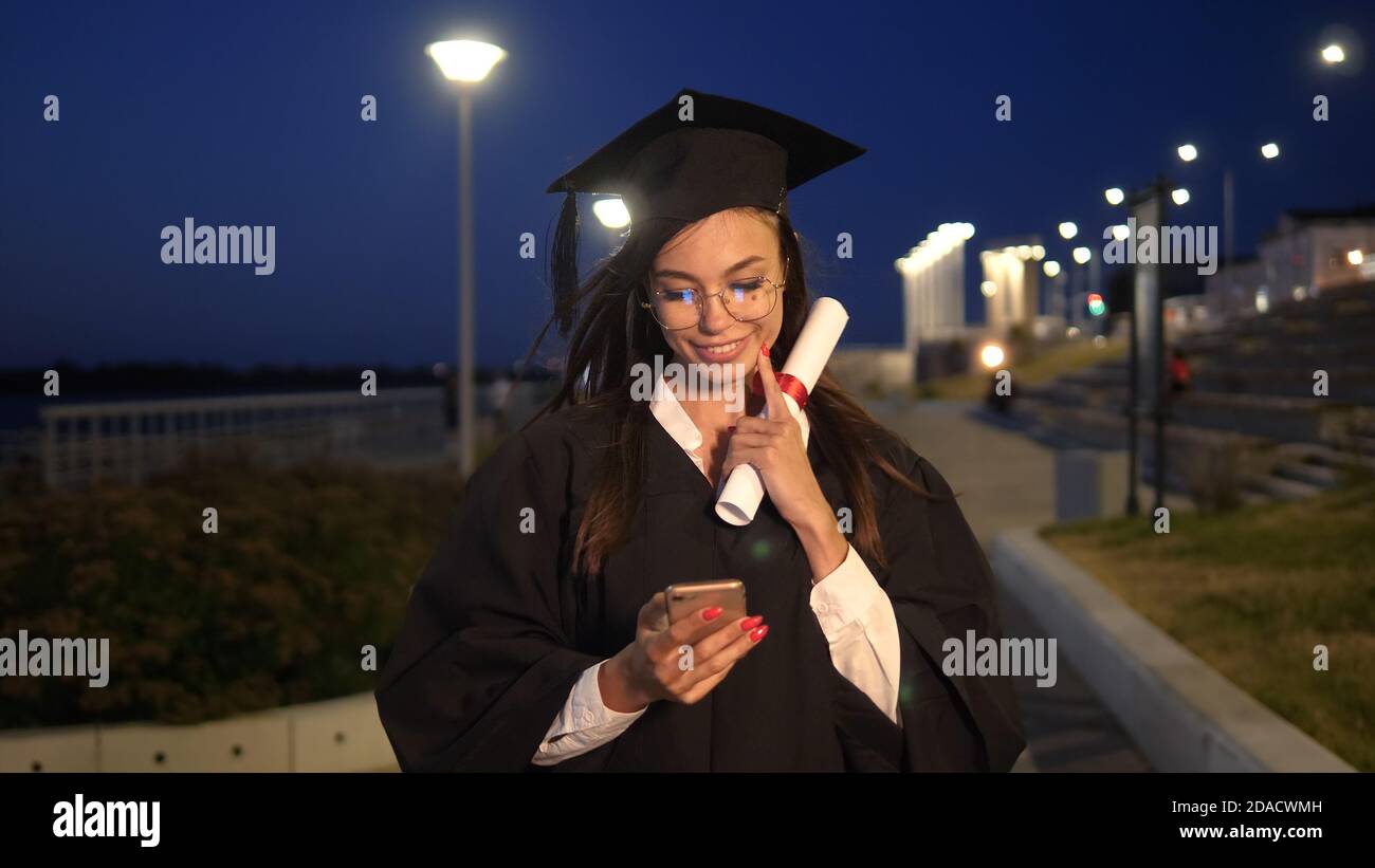 College graduate girl walking with diploma smiling and using her ...