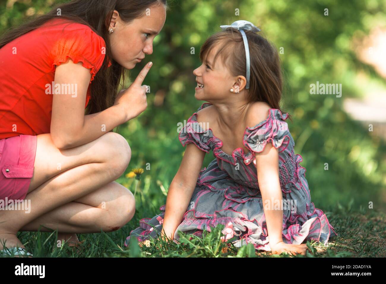 Girl with her finger over her mouth shows for mischievous little sister ...