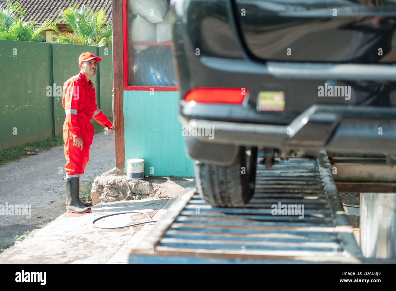 Asian male car cleaner wearing a red uniform and a hat stands looking ...