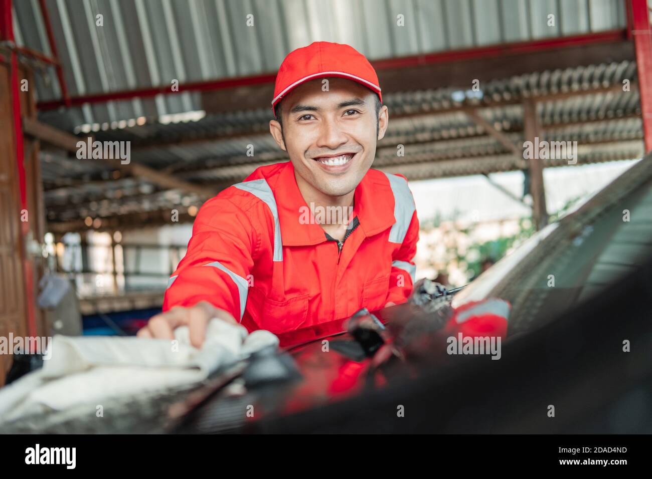 selective focus of car cleaner Asian male wearing red uniform smiling ...