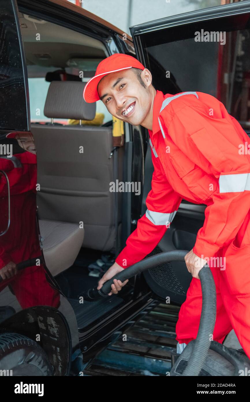 Asian male car cleaner wears red smiling uniform while cleaning car ...