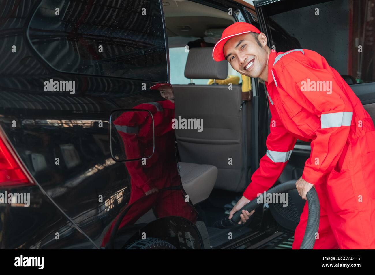 Asian male car cleaner wears red smiling uniform while cleaning car ...