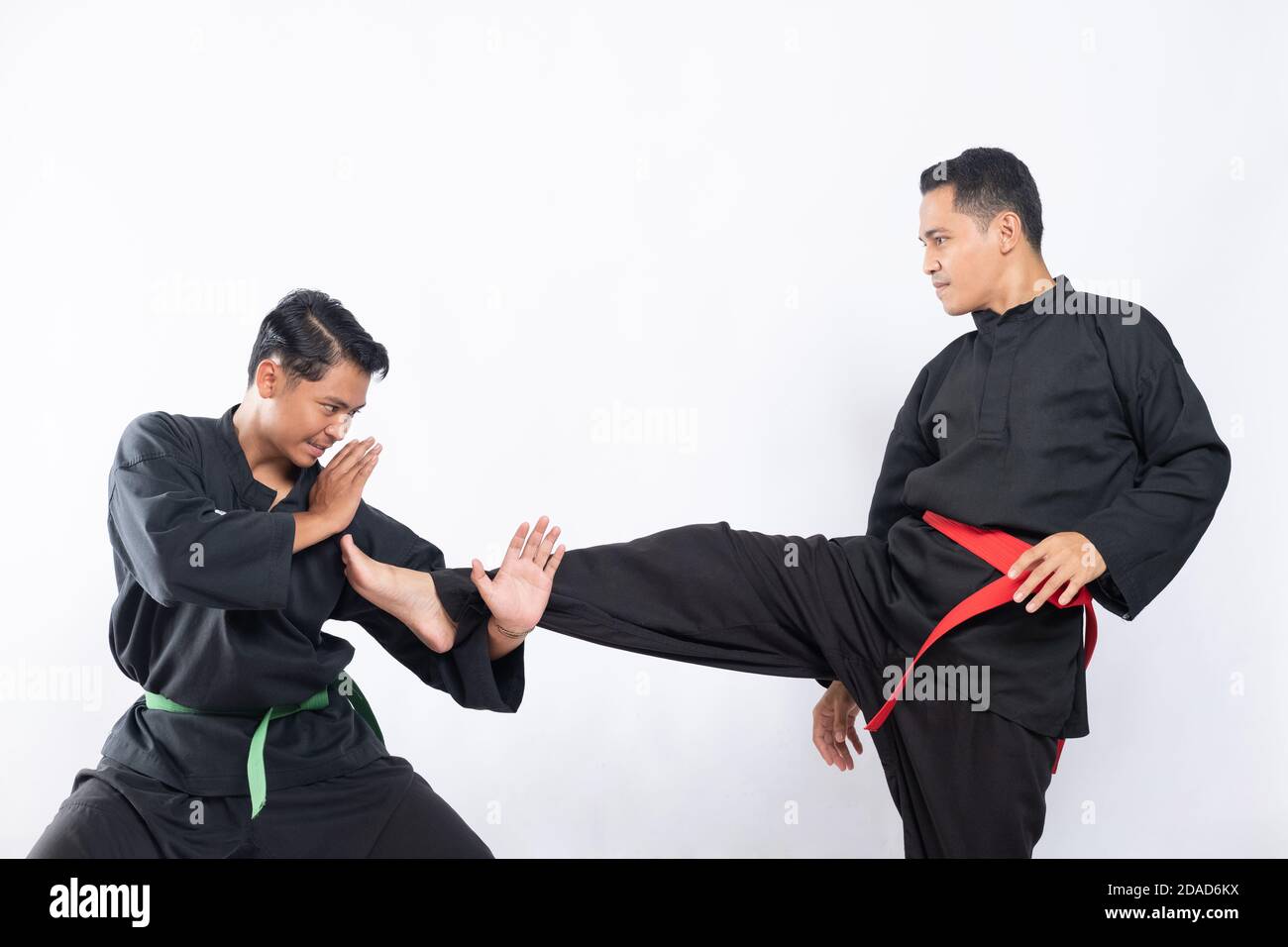 two Asian men wearing pencak silat uniforms fight with tendangan lurus ...