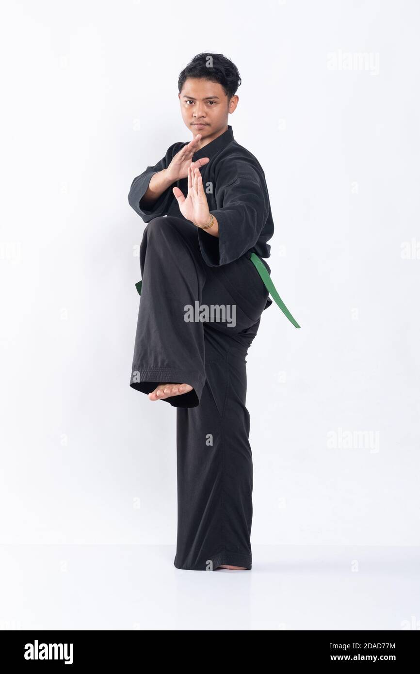 young asian man in pencak silat uniform with one foot raised with both ...