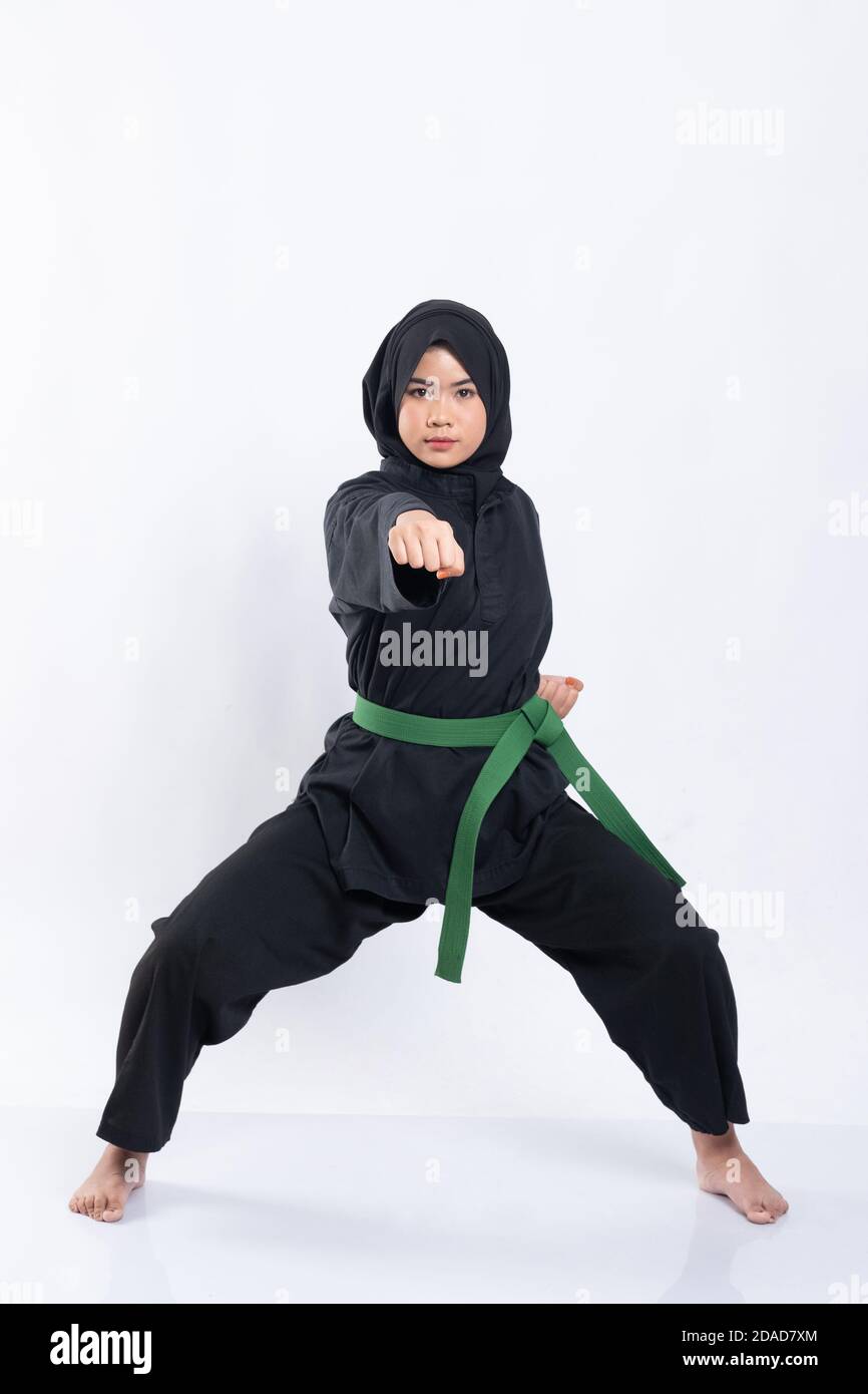 a woman in a veil in a pencak silat uniform poses a middle stance and ...