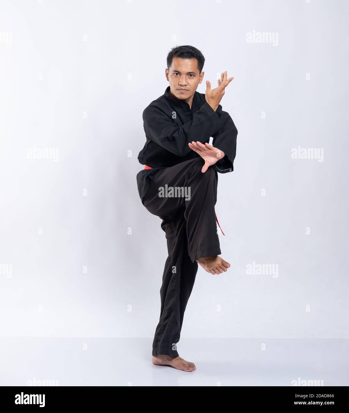 Asian boy with defensive pose raises one leg while wearing a pencak ...