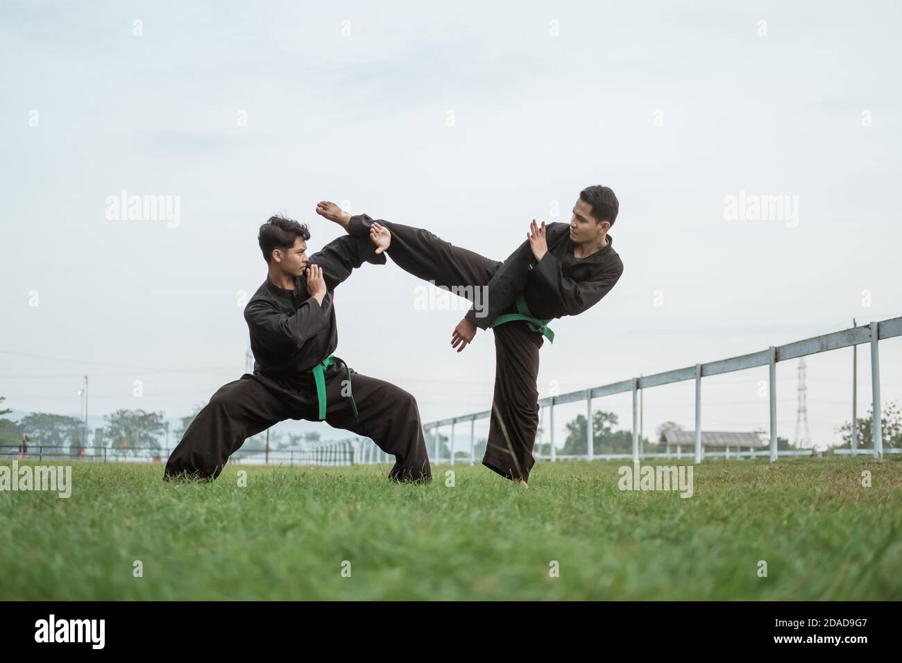 two fighters wearing pencak silat uniforms fighting in an outdoor ...