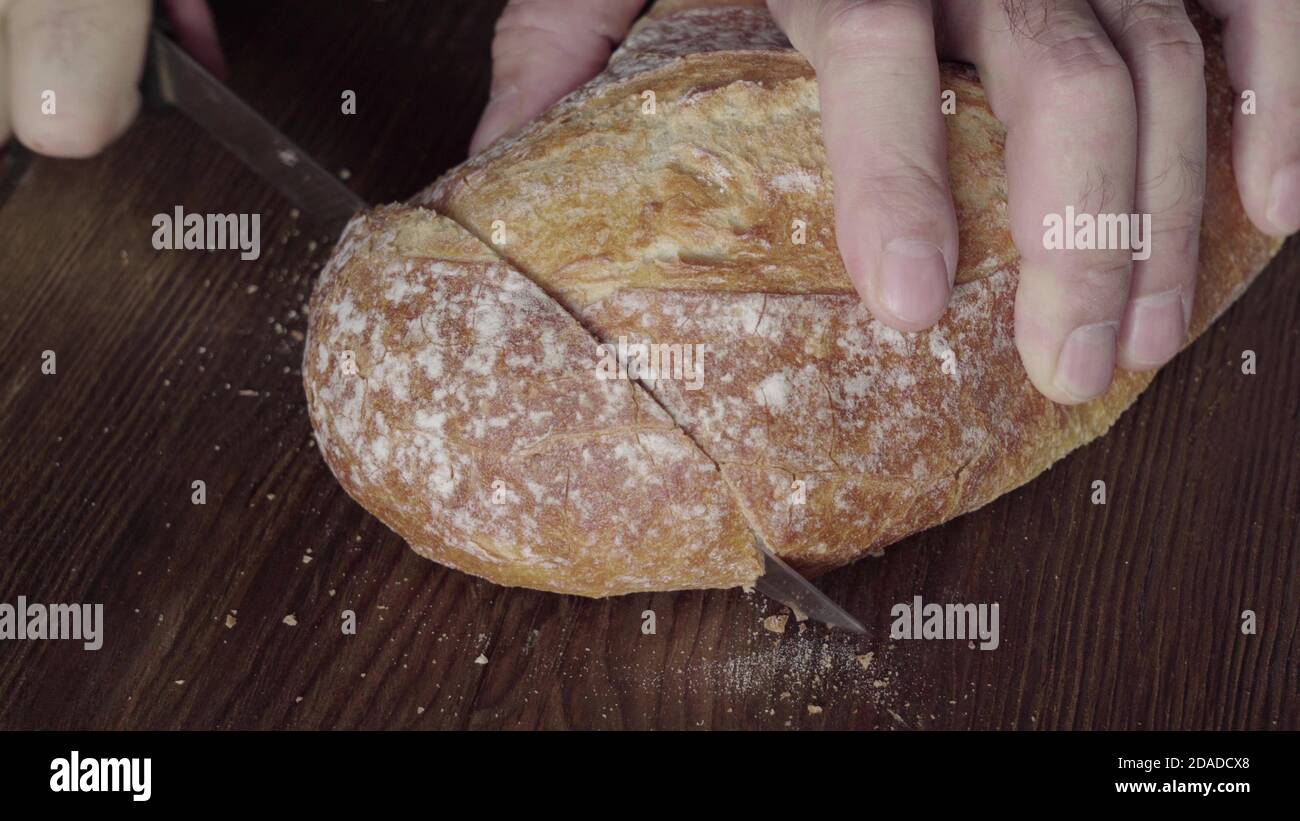 Cutting a loaf of bread on a dark wooden board. Close-up. View from ...