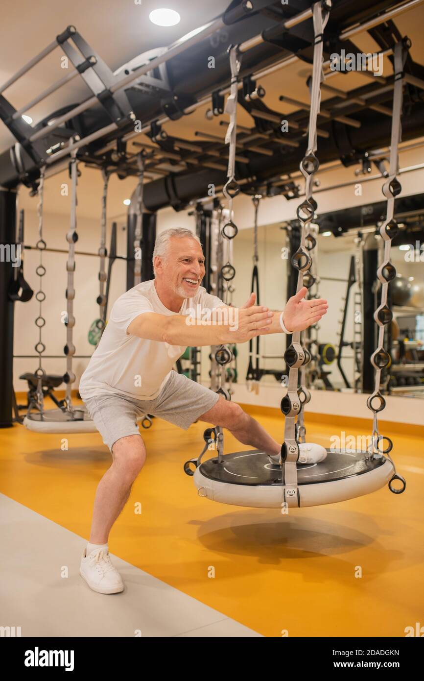 A man doing squats on a hanging gym machine and smiling Stock Photo - Alamy