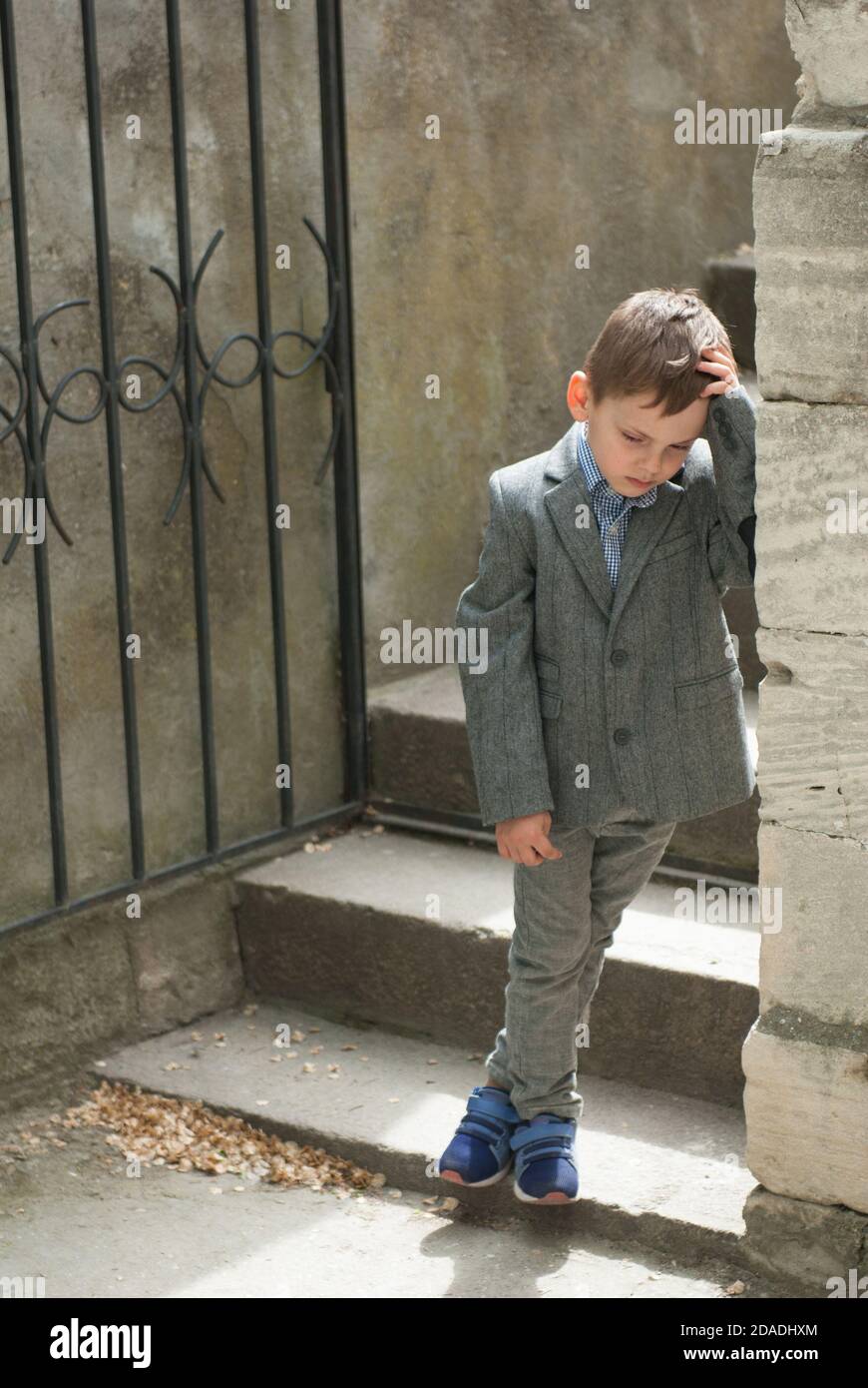 Sad little boy on the background of an old wall and stairs with a gate ...