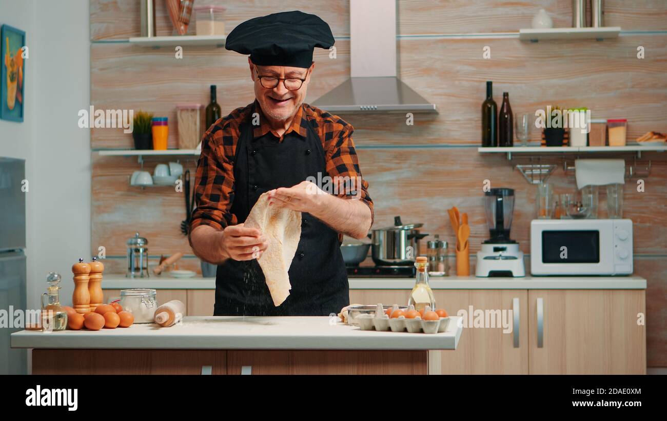 Chef throwing up dough for pizza at home in modern kitchen smilling in ...
