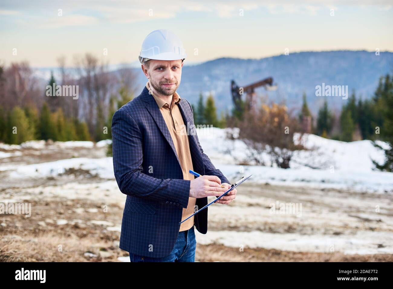 Front view of oil man in protective helmet writing on clipboard while ...