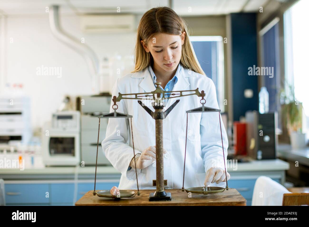 Pretty young female researcher measuring weight of the mineral sample ...