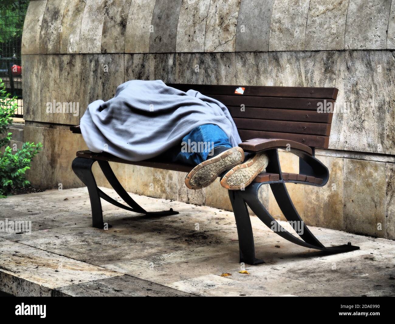 Homeless man with a blanket sleeping on an urban street wooden bench ...
