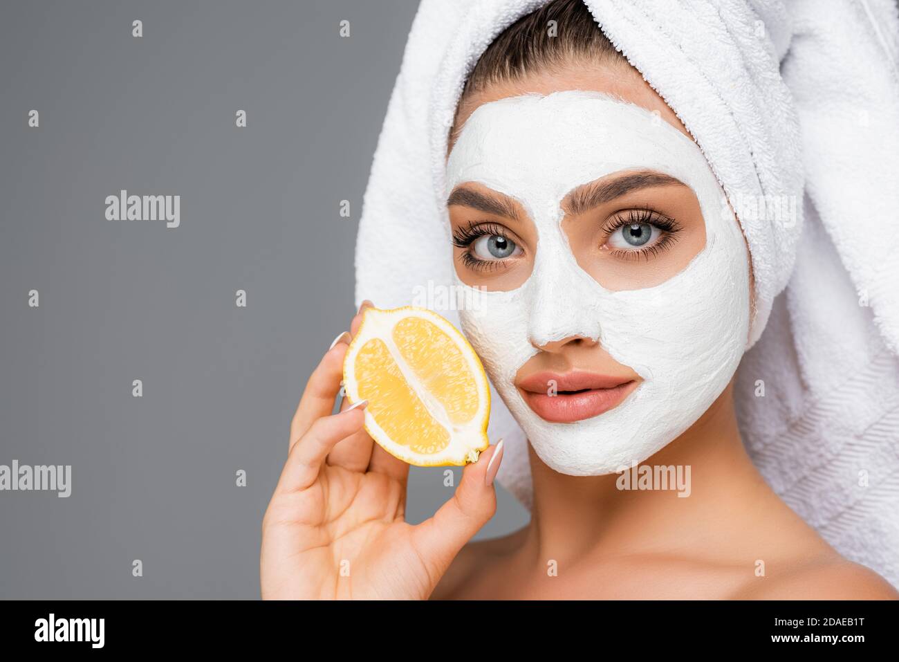 woman with towel on head and clay mask on face holding lemon isolated ...