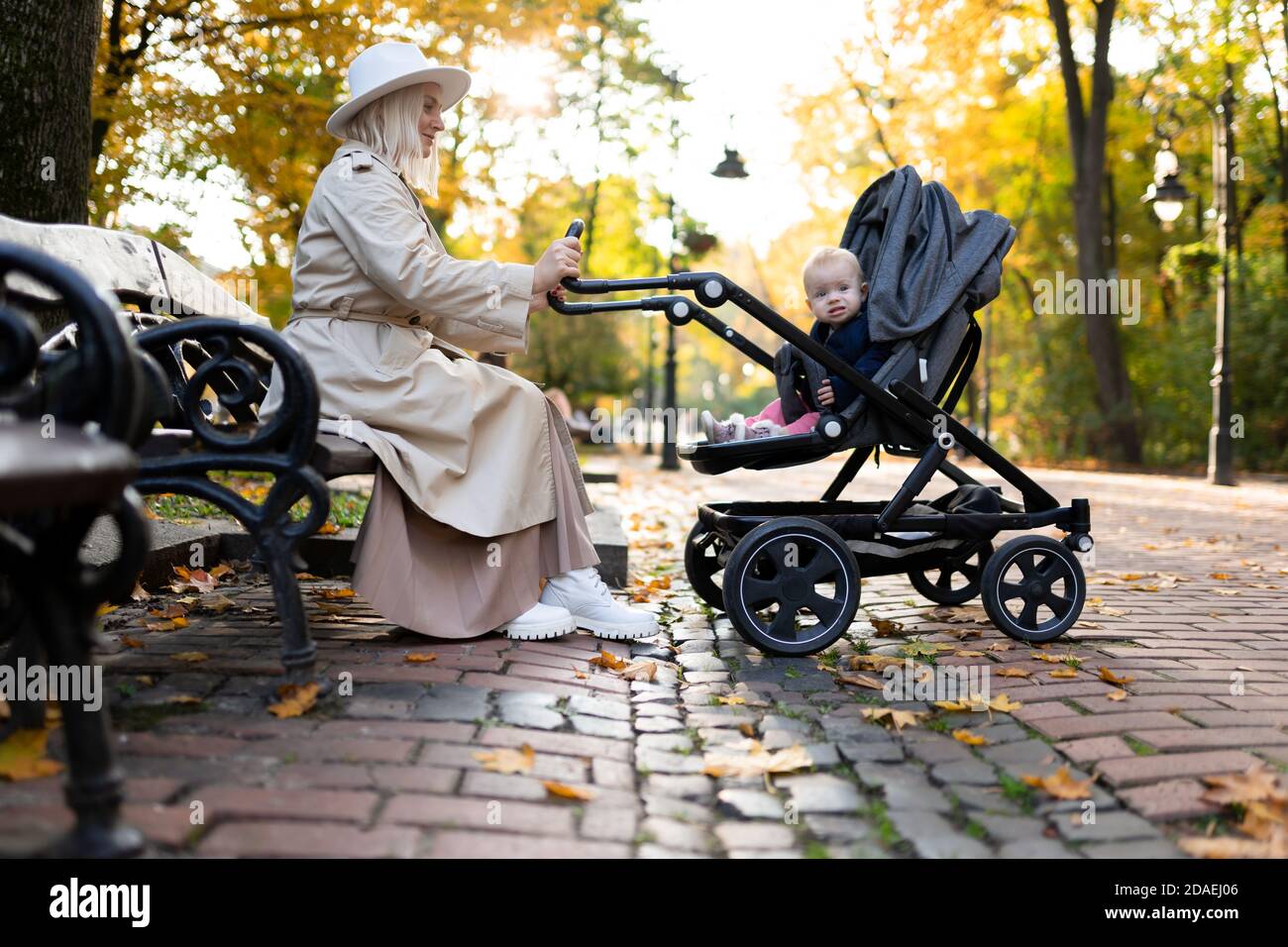 Mother sitting on a bench and rocking the baby in a stroller Stock ...