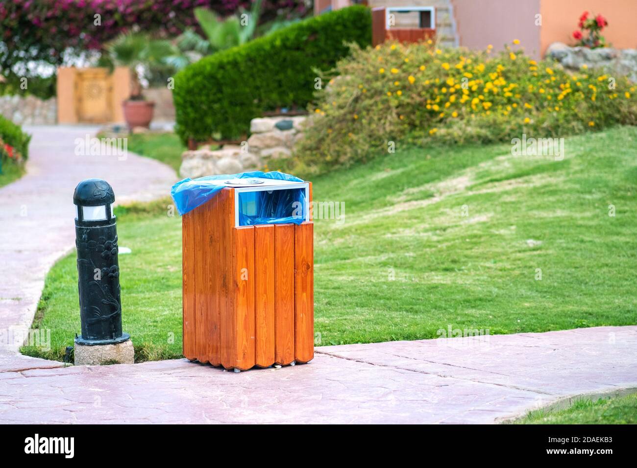 Yellow wooden trash can outdoors on the side of sidewalk in park ...